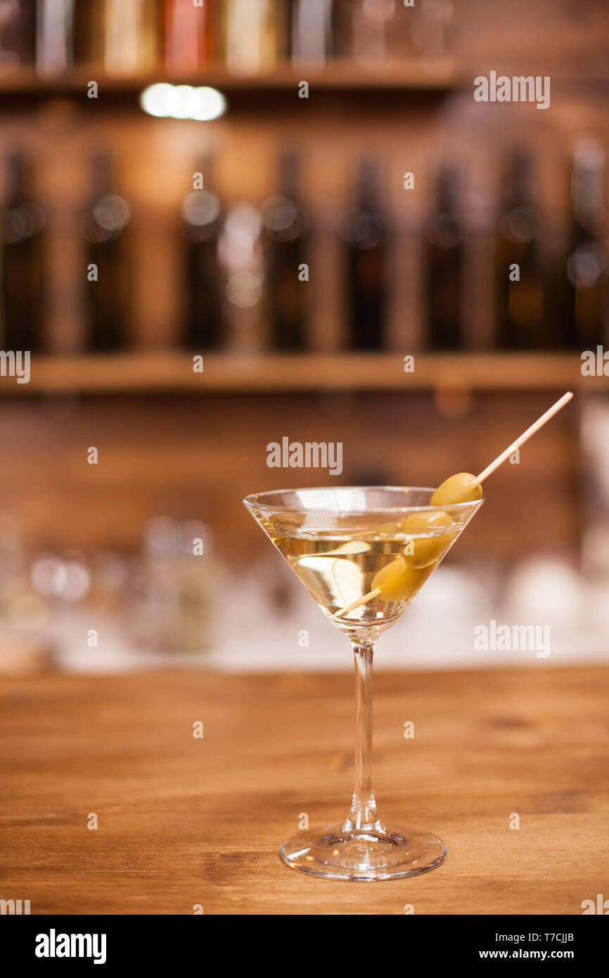 Glass of dry martini with green olives on a rustic wooden bar counter ...