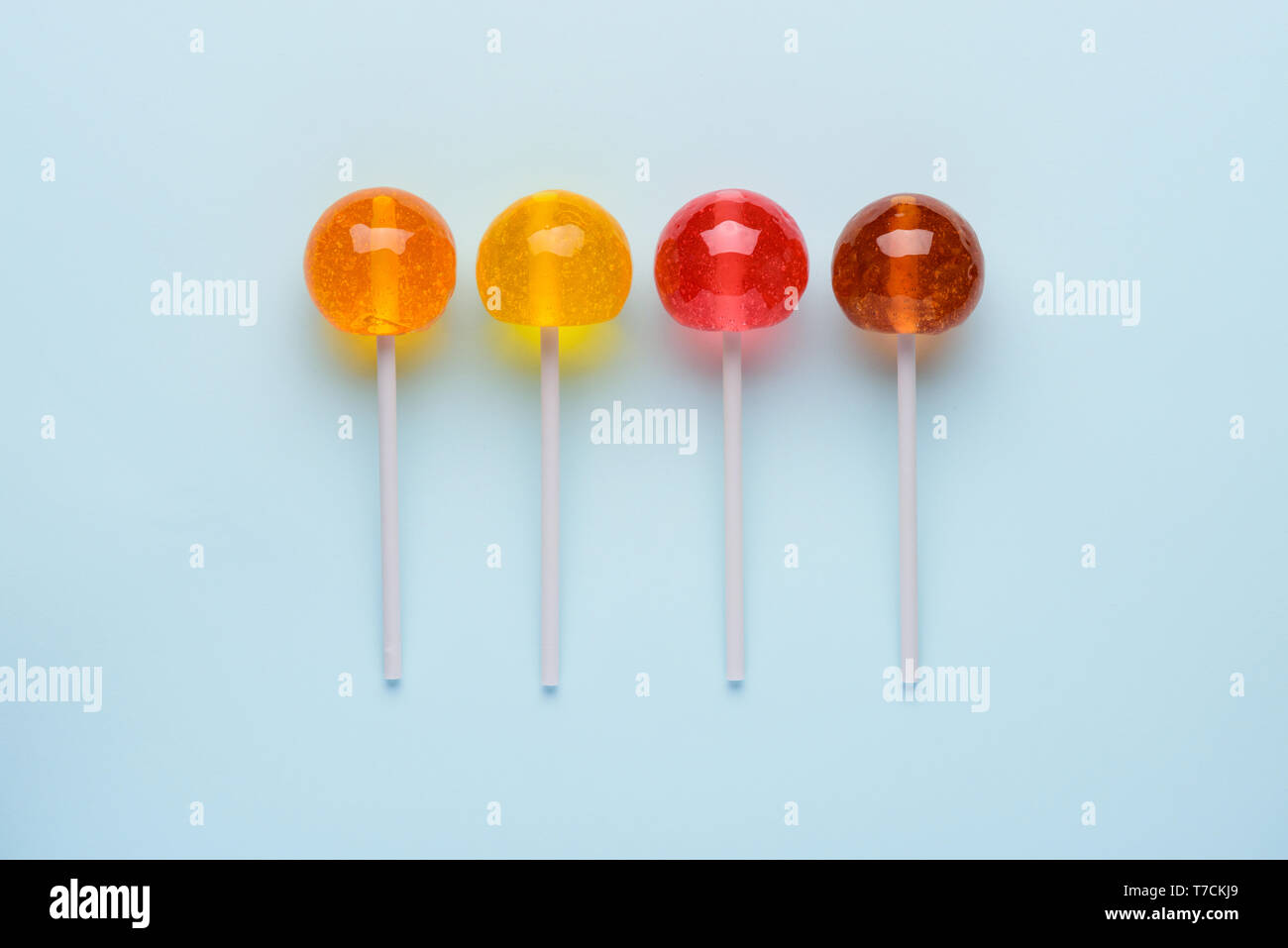 Four different colored and flavoured big shiny lollipops on blue pastel ...