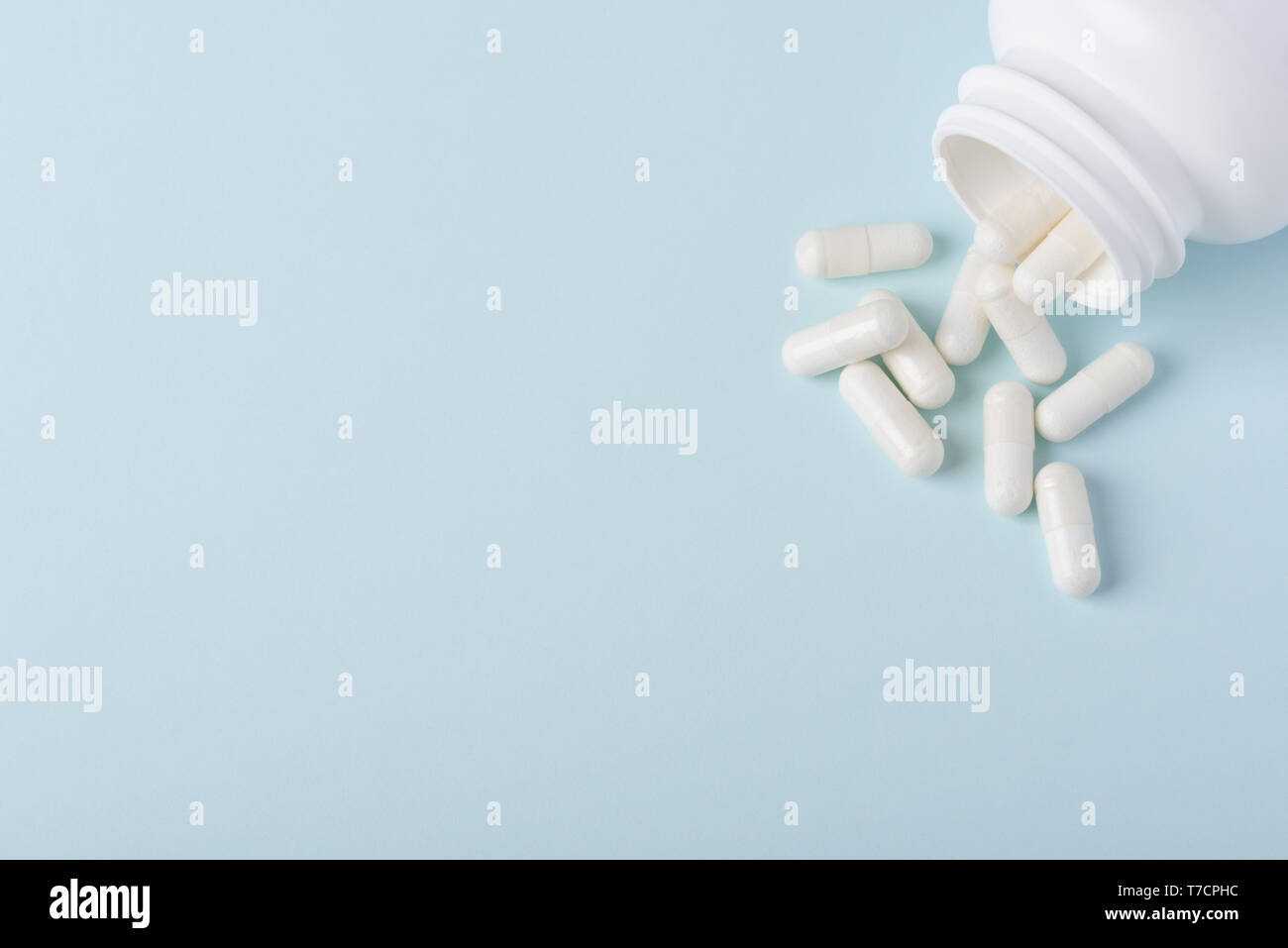 Pills capsules with white powder in white plastic bottle spill on blue ...