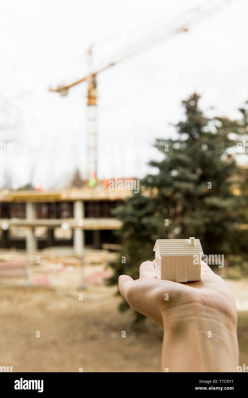 Human hand holding small house model in front of construction site ...