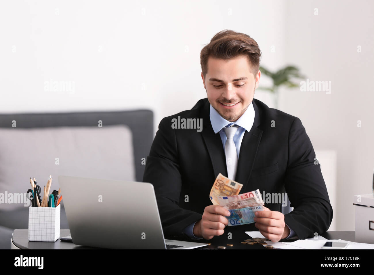 Young businessman counting money at table indoors. Money savings ...