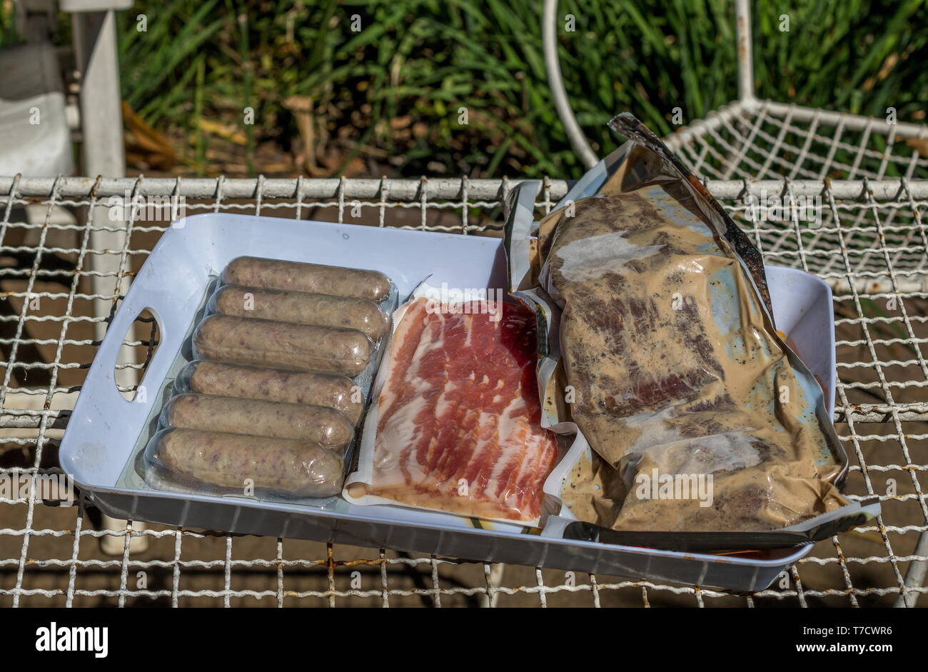 Fresh raw frozen meat thawing in the sun outdoors on a garden table in ...