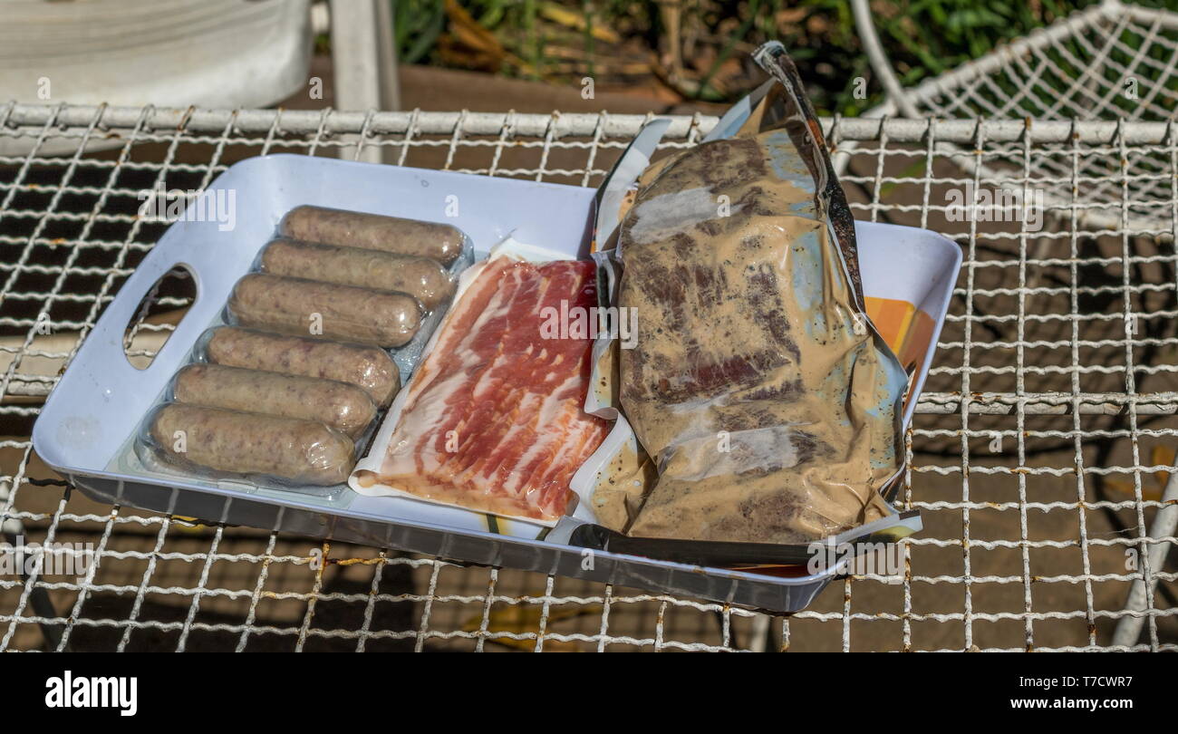 Fresh raw frozen meat thawing in the sun outdoors on a garden table in ...