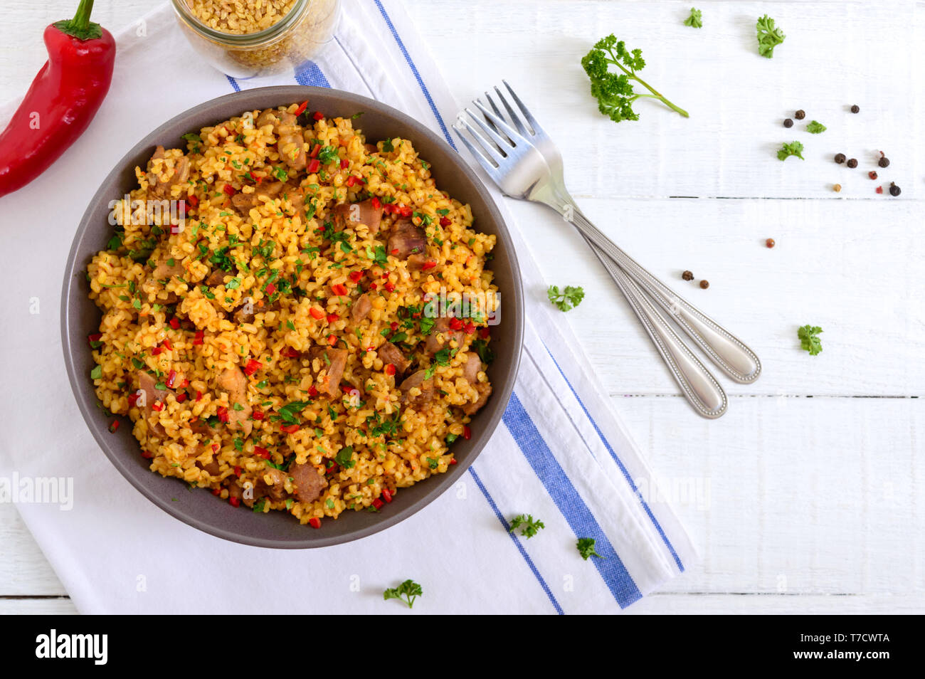 Delicious bulgur with vegetables, meat and greens on a white wooden ...