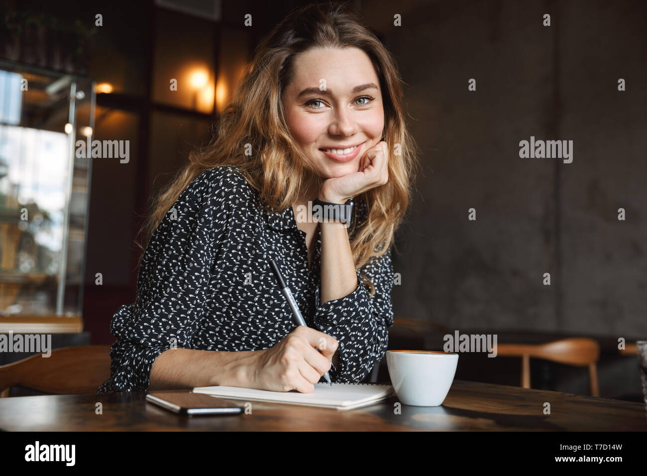 Photo of beautiful young pretty woman sitting in cafe indoors writing ...