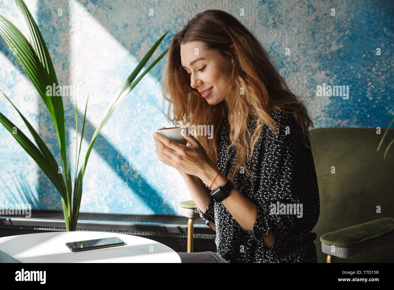 Photo of beautiful young pretty woman sitting in cafe indoors drinking ...