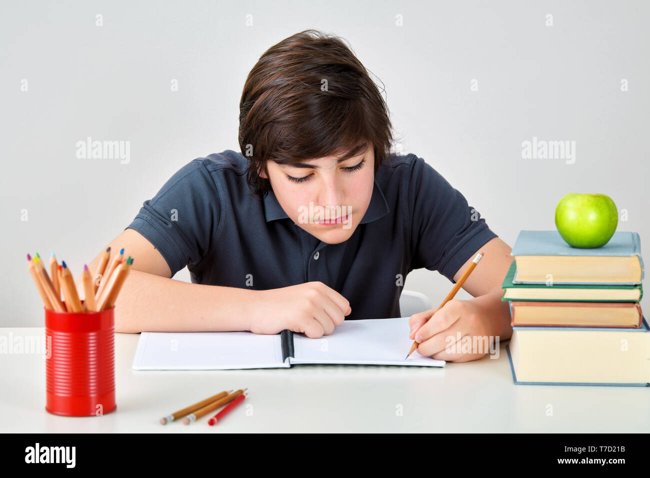 Caucasian teenager boy sitting at the table writing to his notebook ...