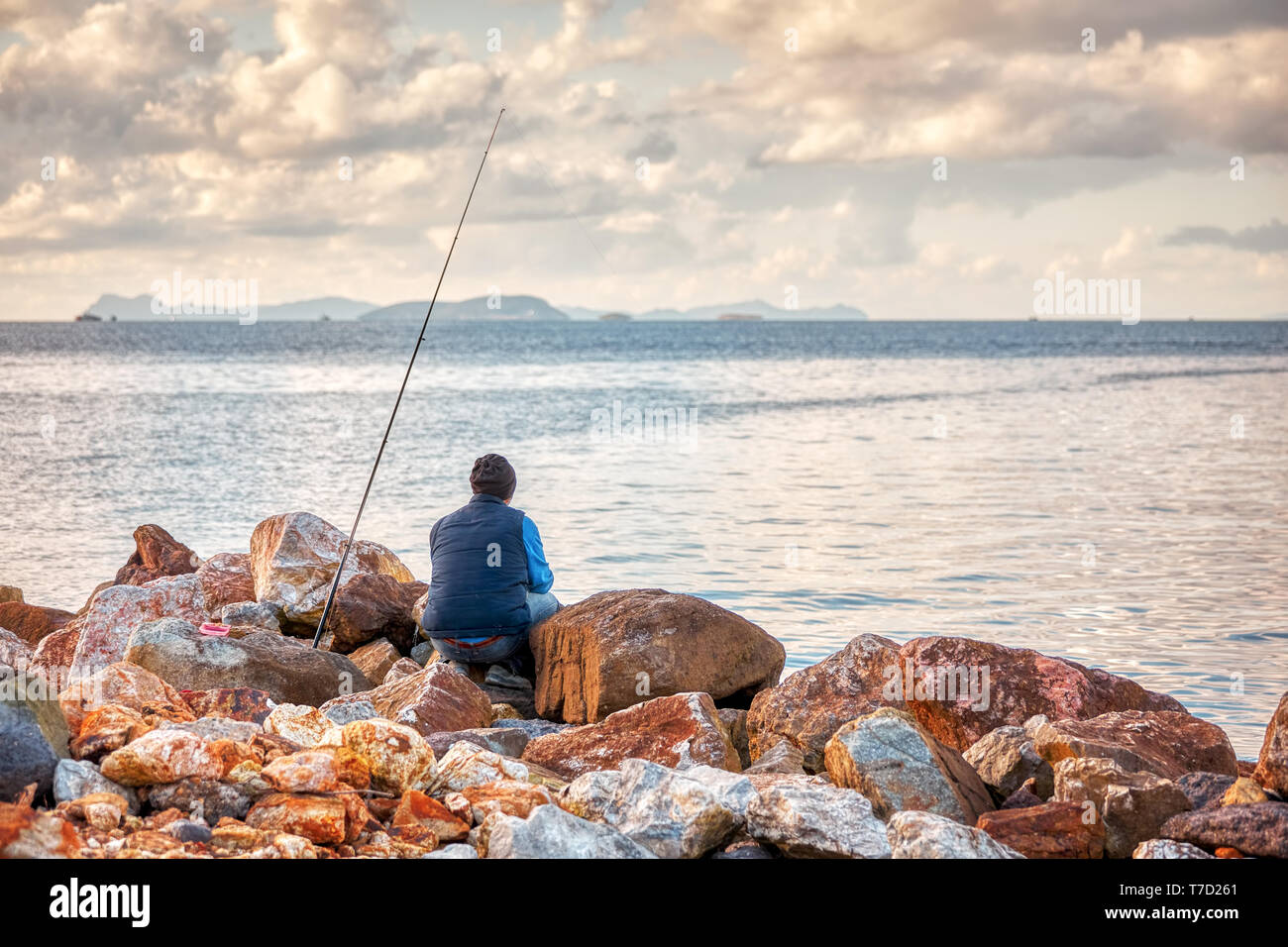 Facing back crouched angler fishing with his rod on the rocks at the ...