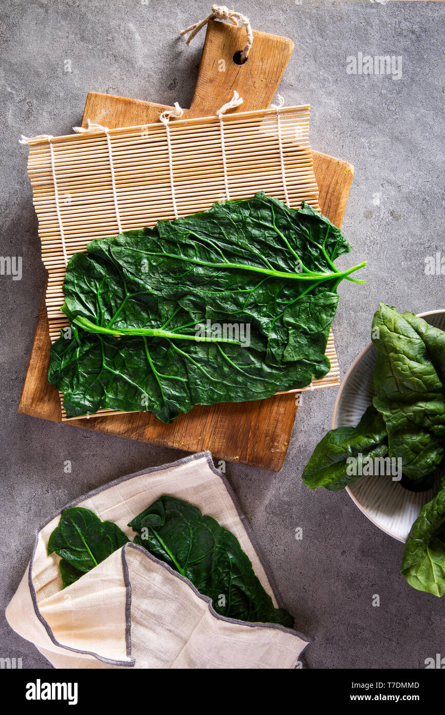 Vegan maki sushi with spinach coating in the making on wooden board ...