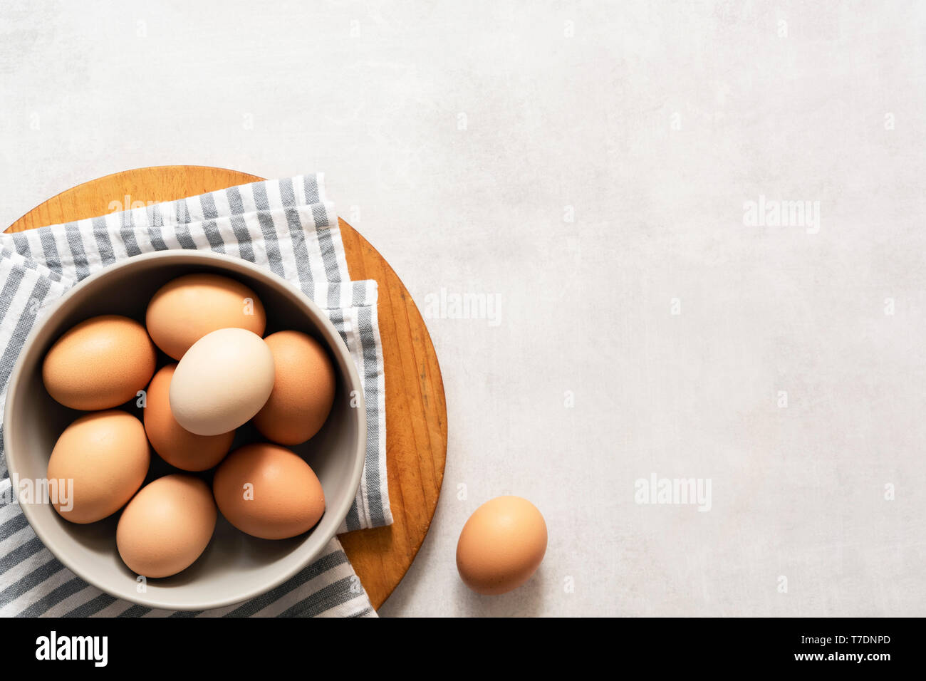 Fresh hen eggs in a bowl on a textured grey background with copyspace ...