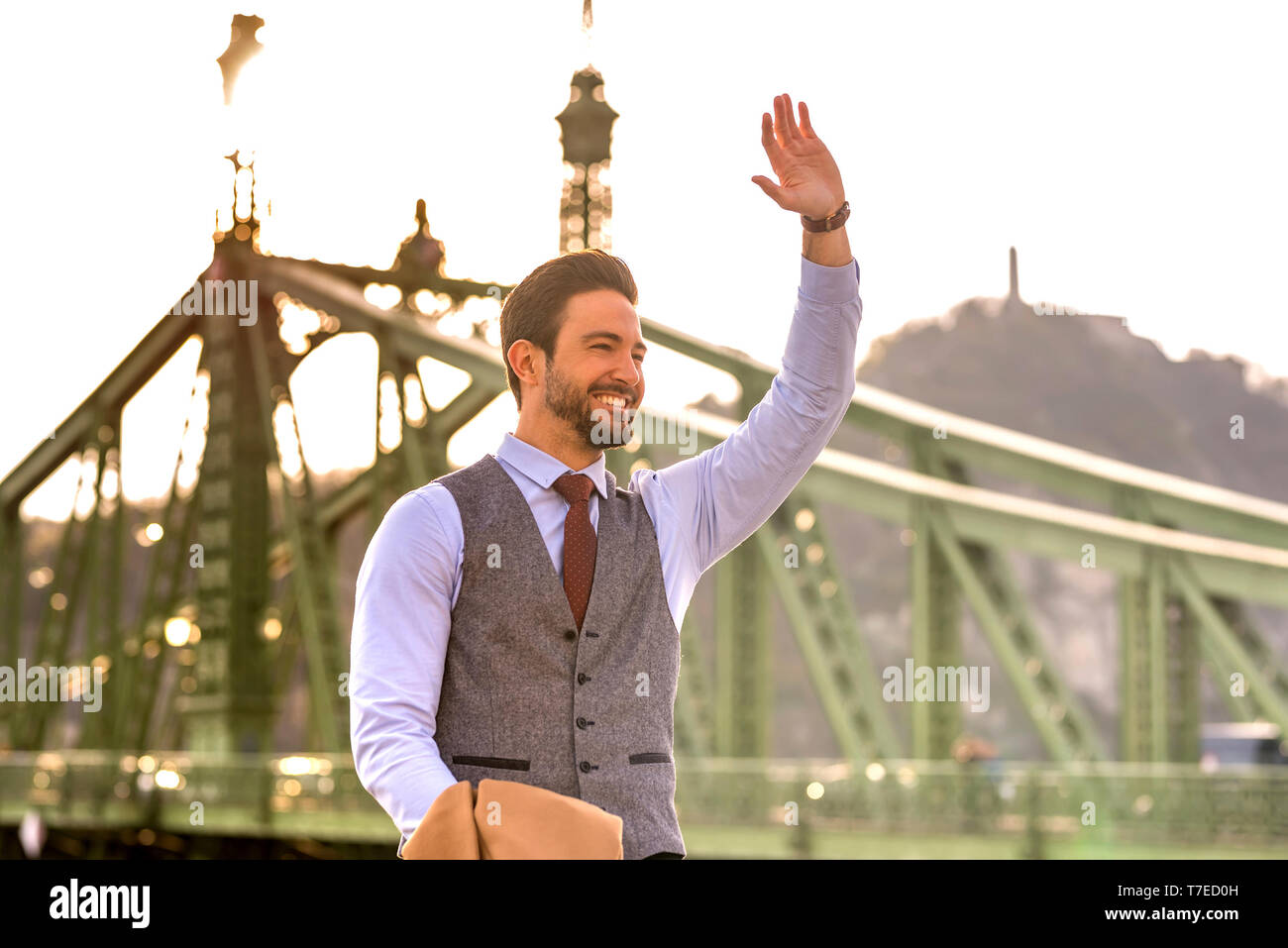 A handsome elegant man standing next to a river and waving with his ...