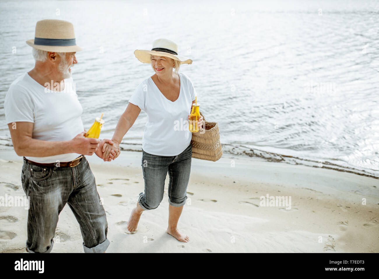 Happy senior couple dressed in white t-shirts and hats walking together ...