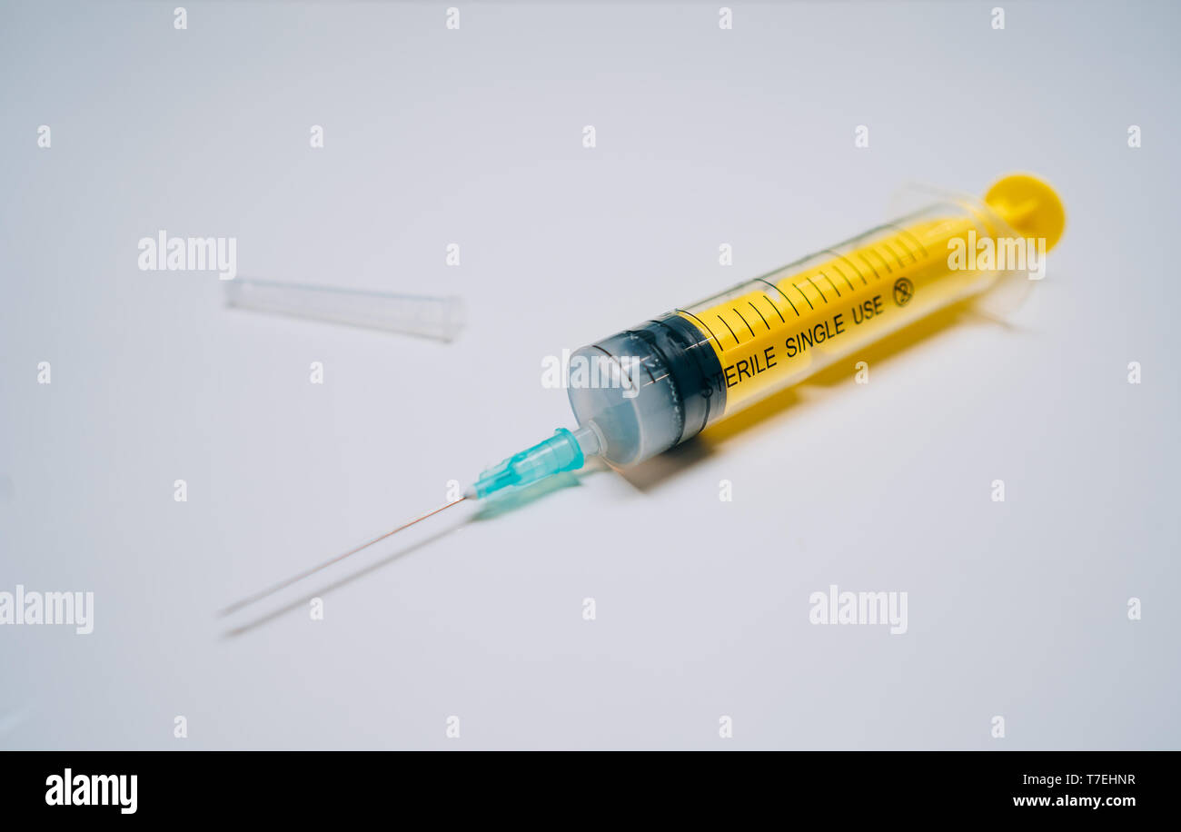 One one-off yellow medical syringe with the drug lying over white table ...