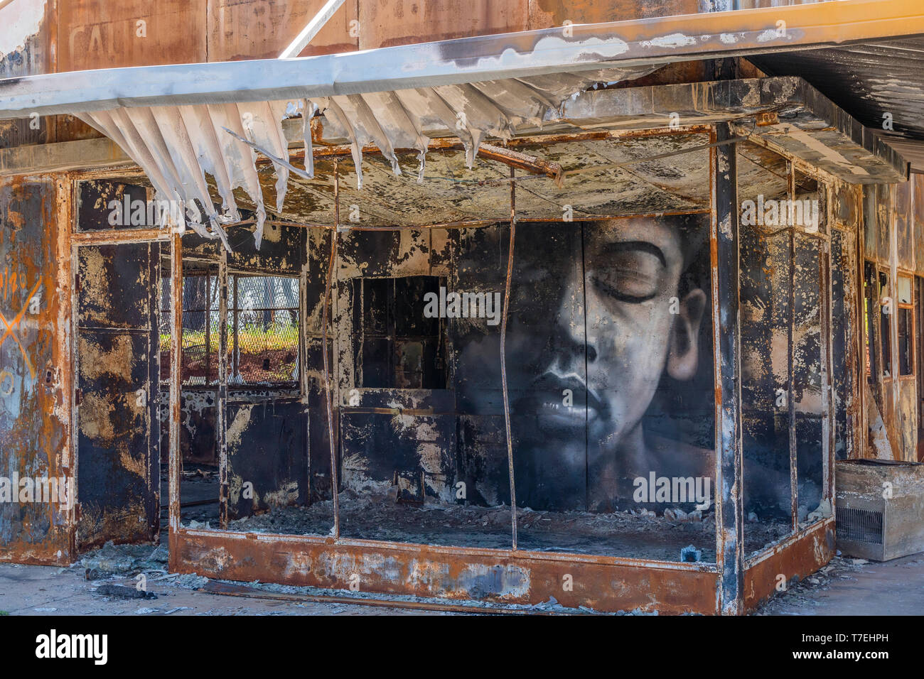 A building gutted by wildfire has a large face painted on an inside ...
