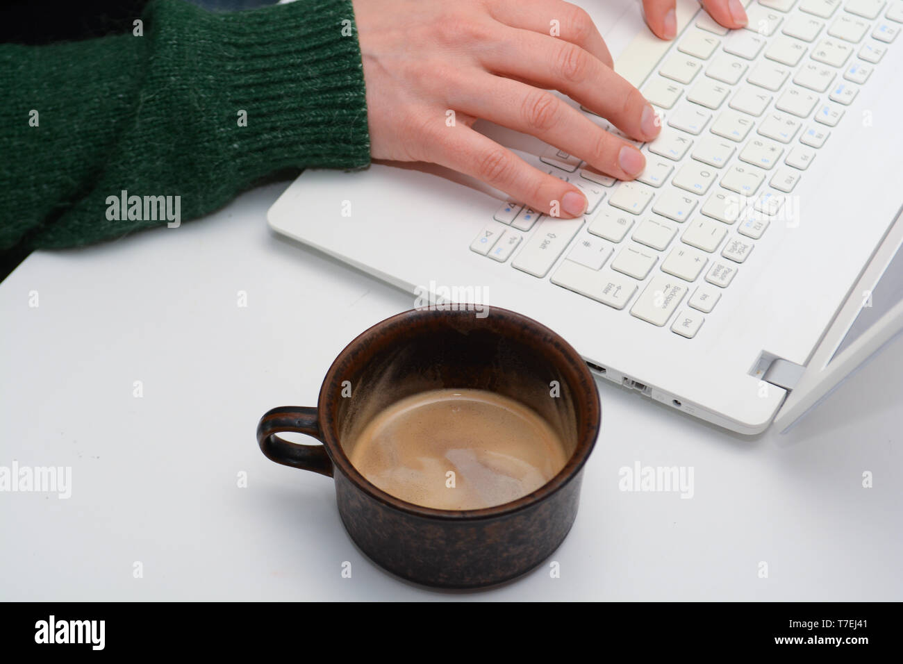 A woman using a laptop computer sitting at a white desk Stock Photo - Alamy
