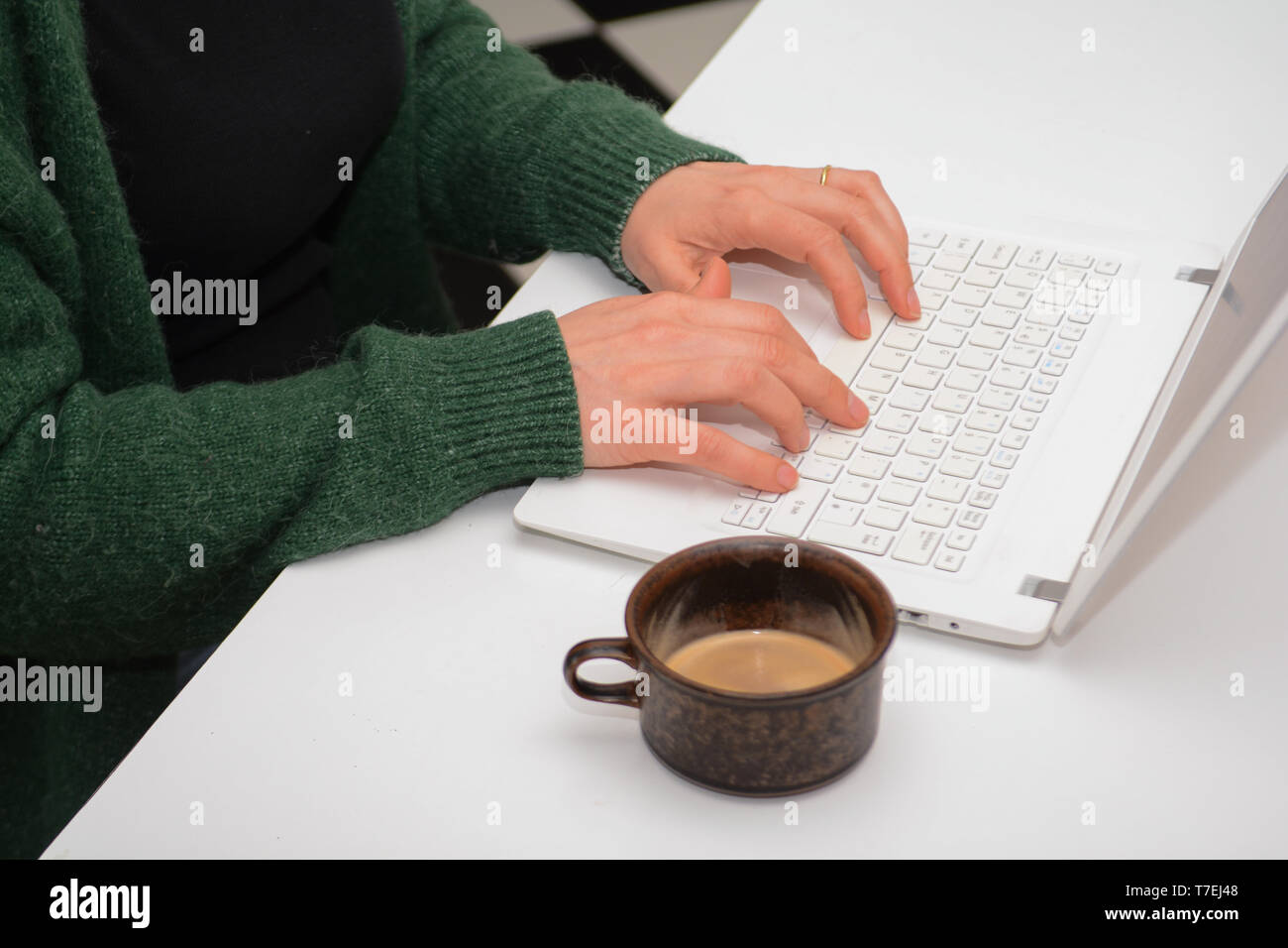 A woman using a laptop computer sitting at a white desk Stock Photo - Alamy