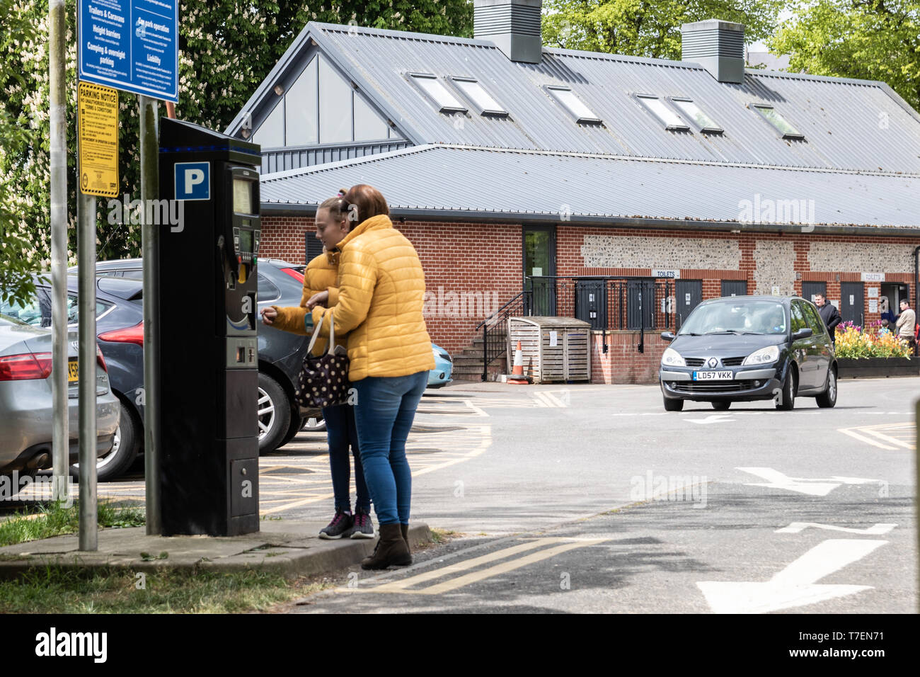 Mother and daughter using a pay and display parking meter in a car park ...