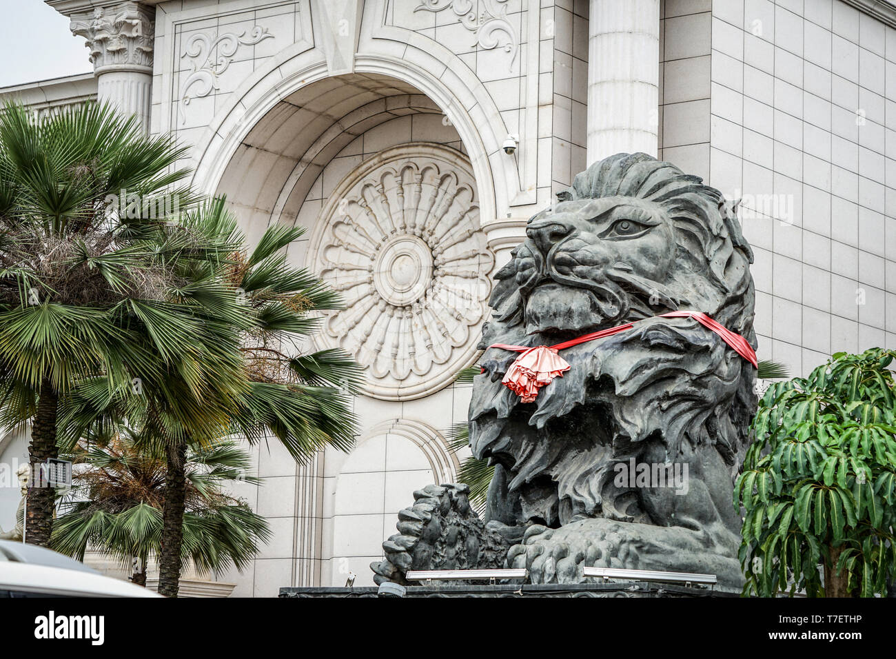 close up big black lion statue with red scarf sitting front of building ...