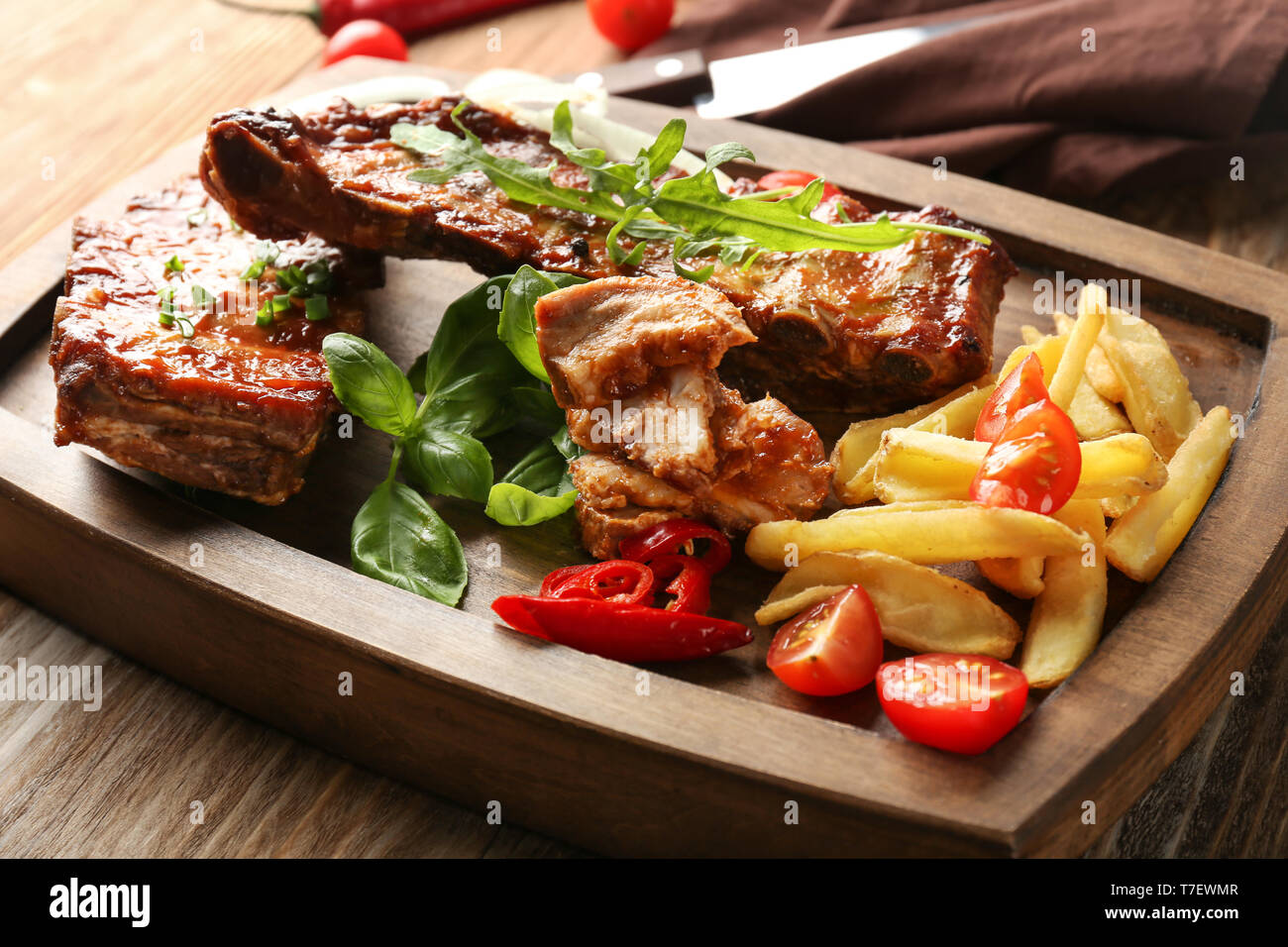 Wooden board with delicious grilled ribs and french fries on table ...