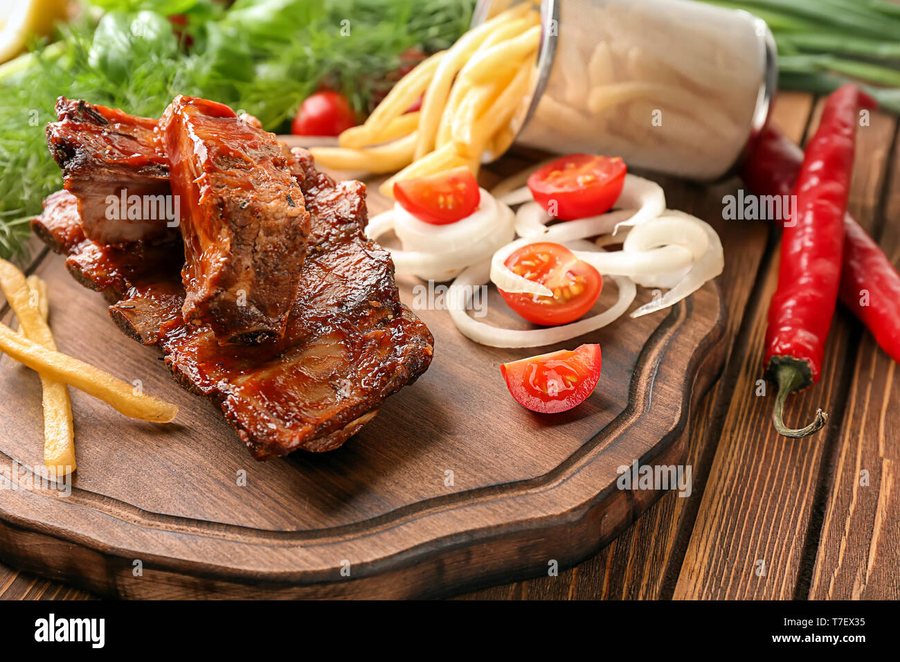 Wooden board with delicious grilled ribs and french fries on table ...