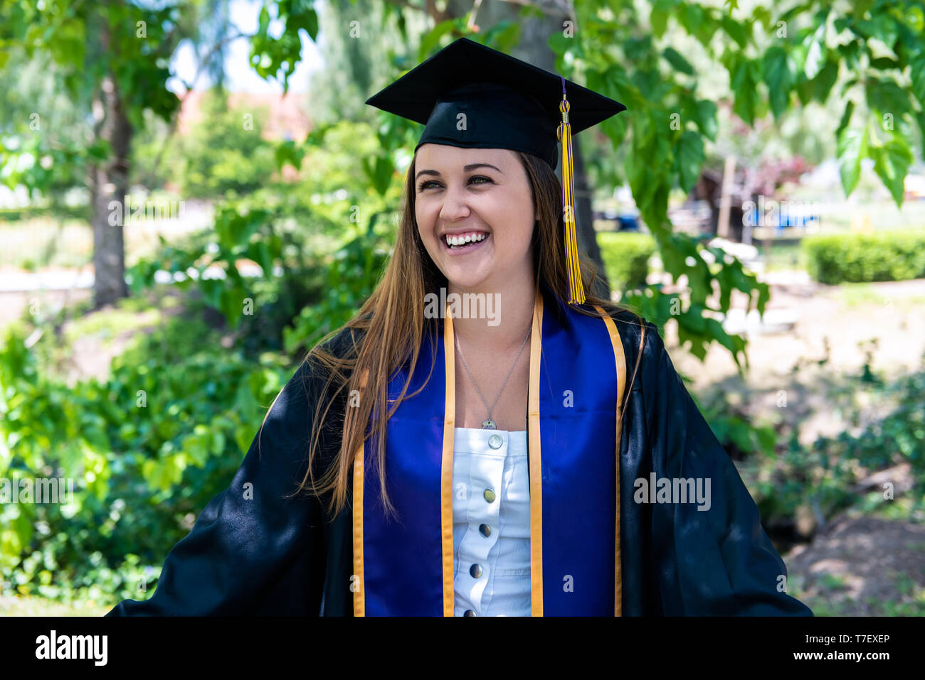Beautiful young and happy female student standing behind campus bench ...