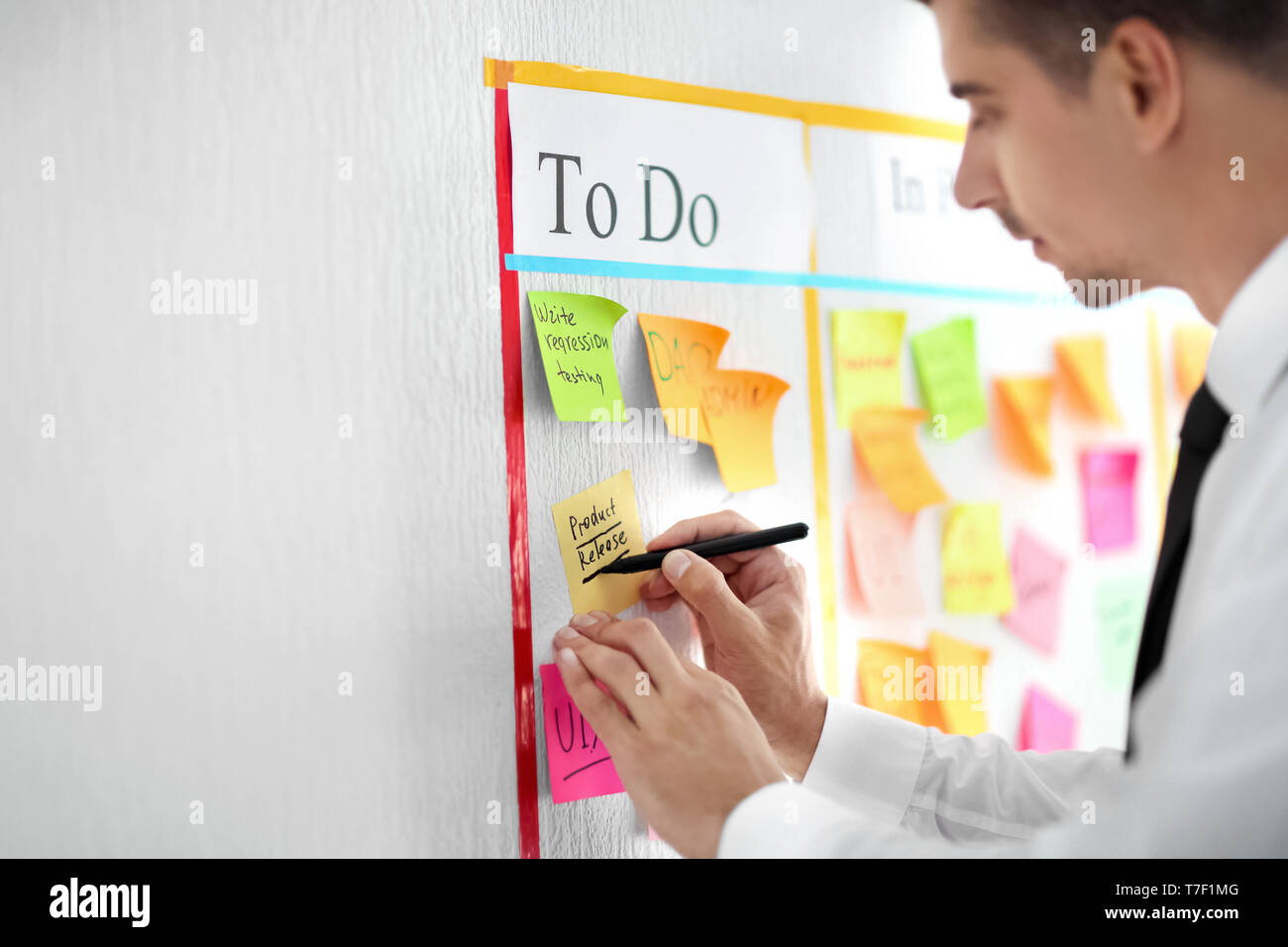 Man writing on sticky note attached to scrum task board in office Stock ...