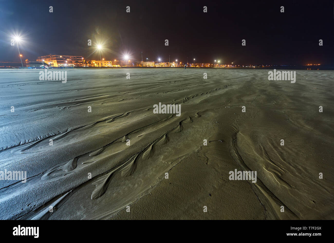 Water receding at low tide with textured lines in the sand and evening ...