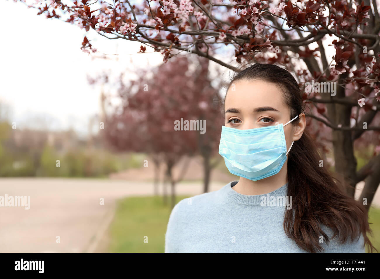 Young woman in protective mask near blooming tree. Allergy concept ...
