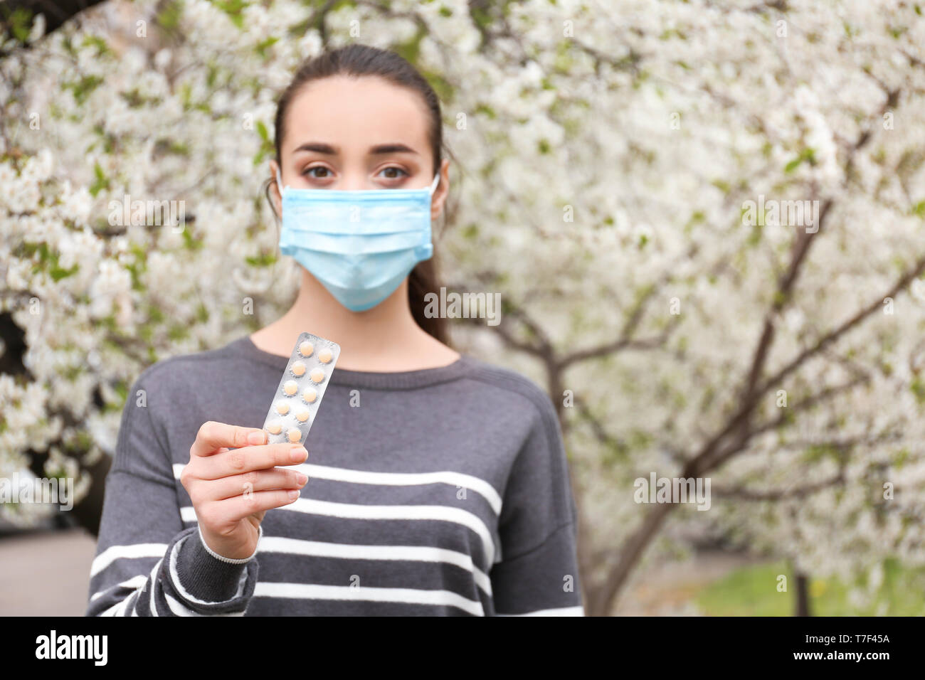 Young woman in protective mask holding pills near blooming tree ...