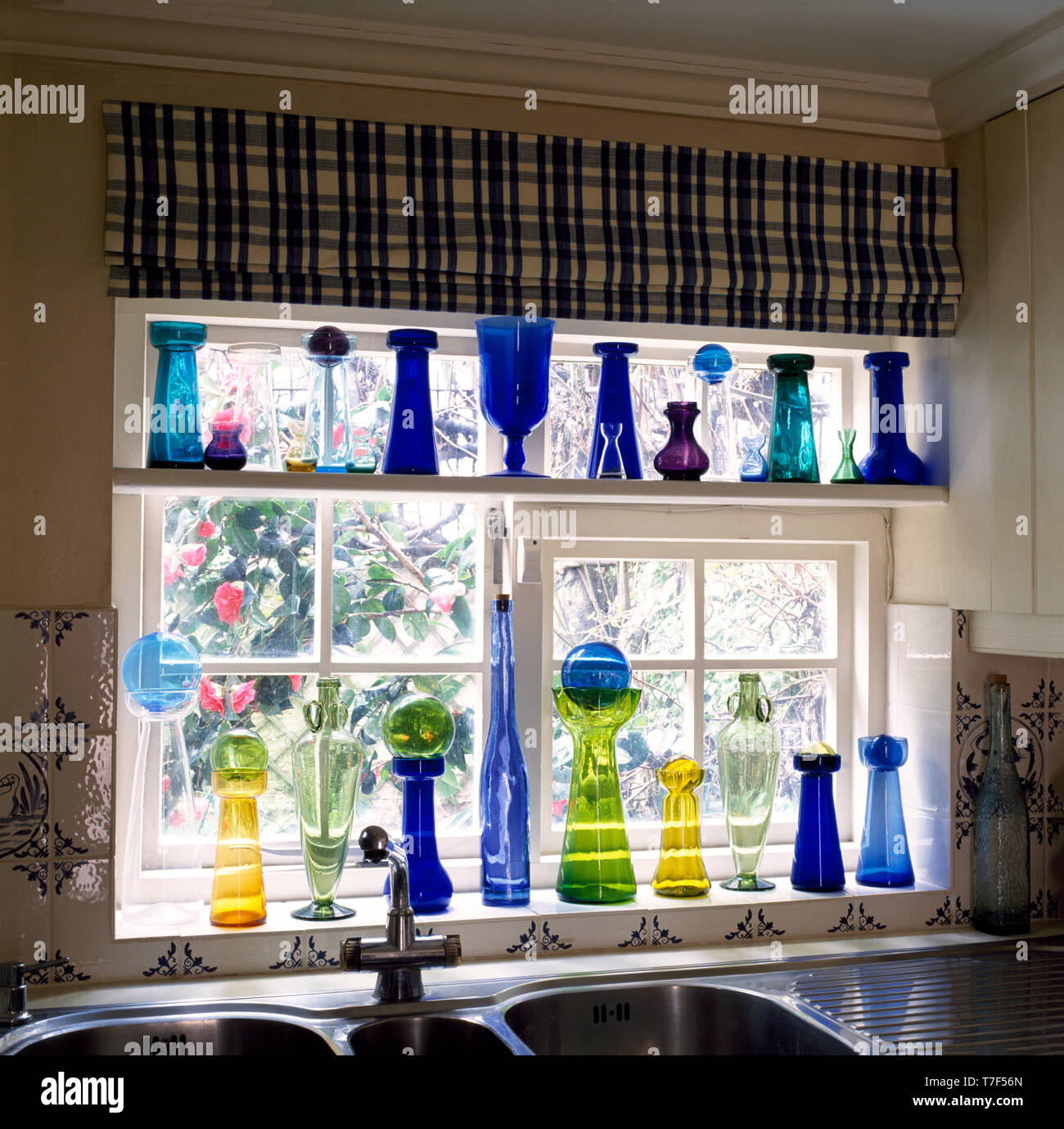 Checked blind on window with collection of glassware on shelf Stock ...