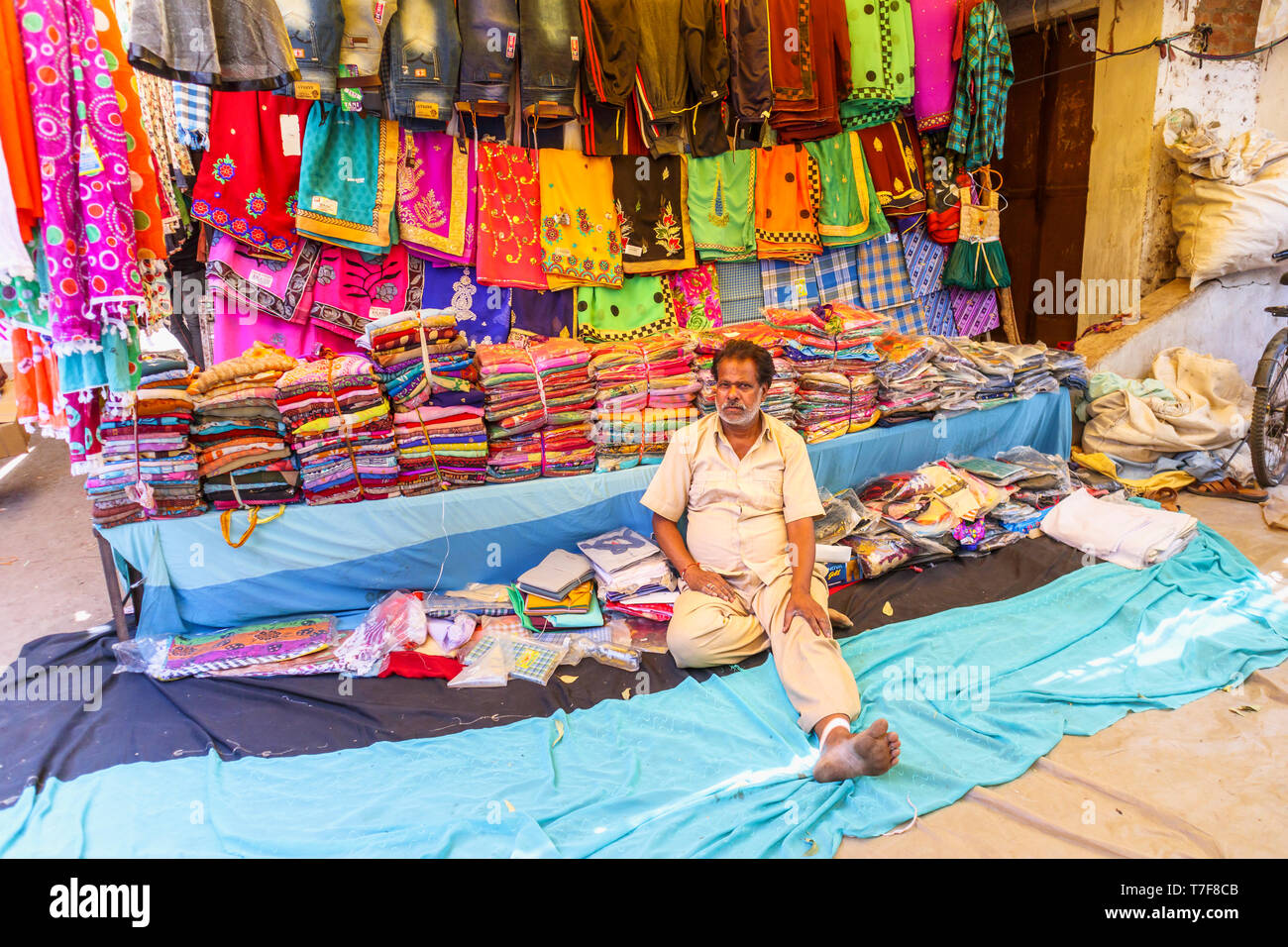Stallholder sitting at a stall selling fabrics in a local indoor market ...