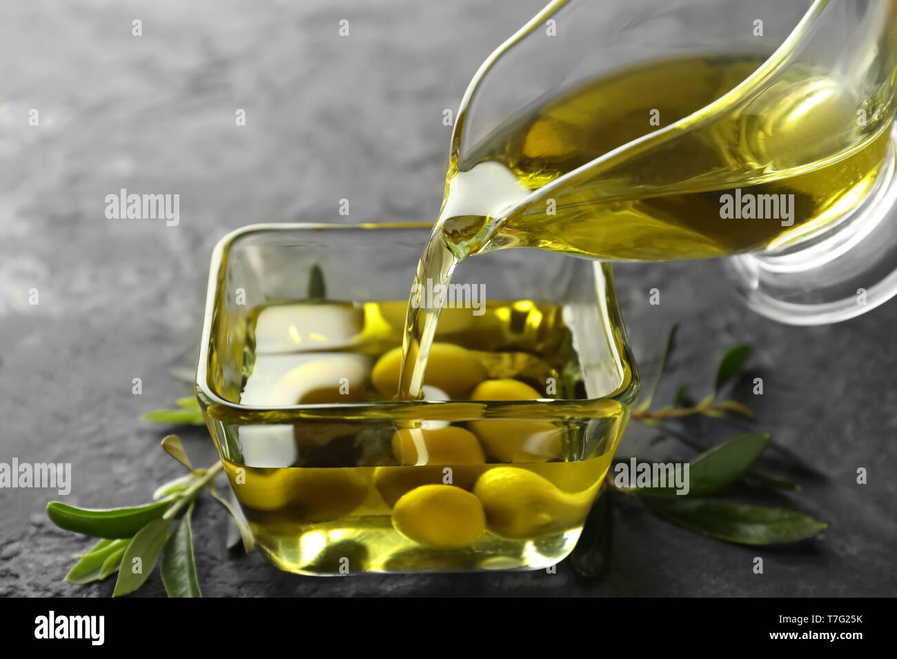 Pouring of fresh oil into bowl with olives on table Stock Photo - Alamy