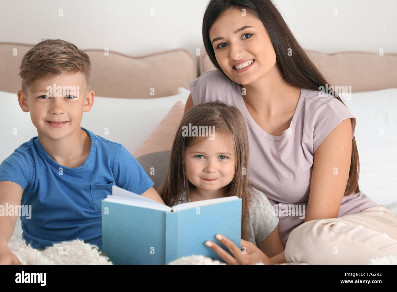 Mother and her children reading book together at home Stock Photo - Alamy