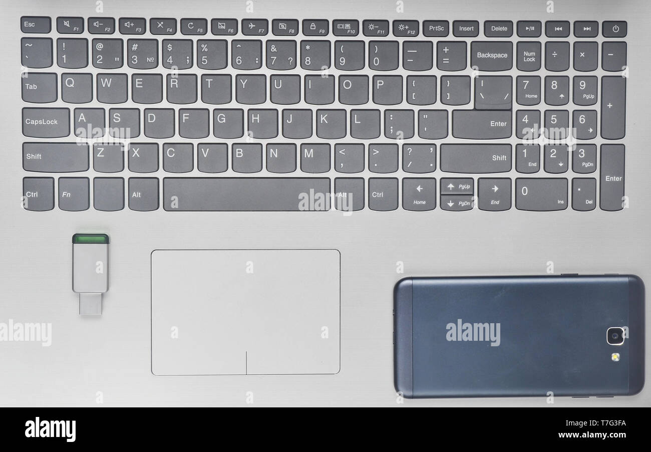 Smartphone, usb flash drive on laptop keyboard. Top view. Modern ...