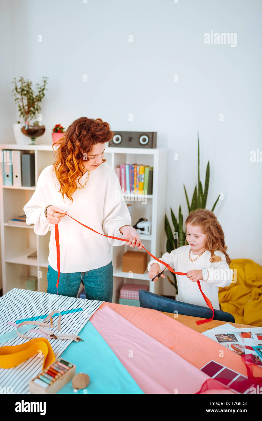 Little girl cutting red ribbon with her mother designing clothes Stock ...