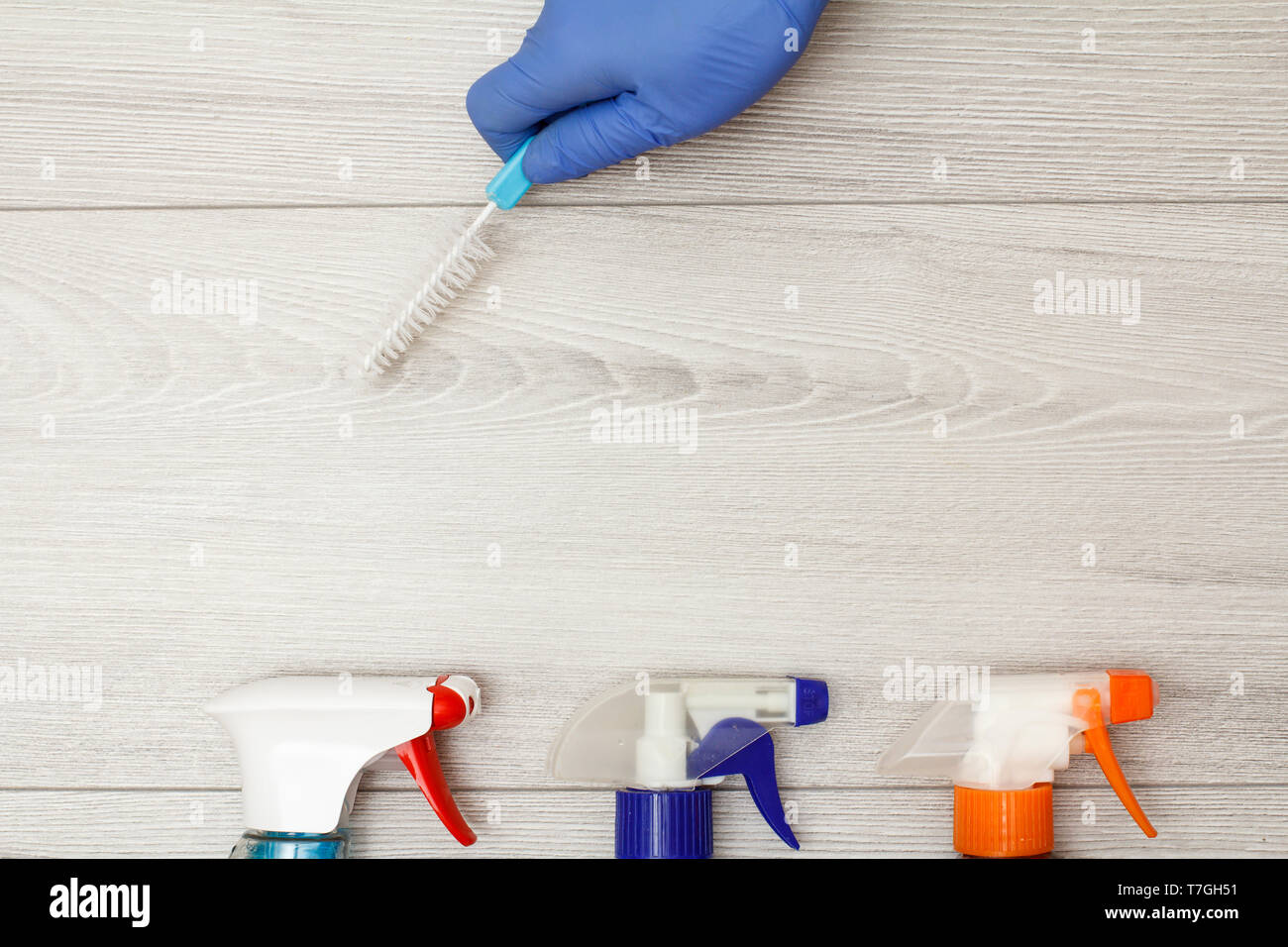 Hand in rubber glove holding dust brush with bottles of detergent on ...