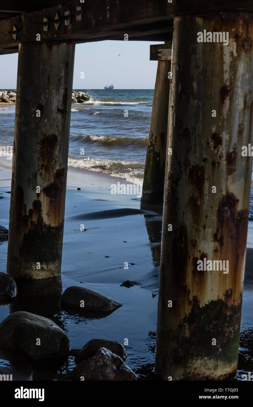 Cargo ship on the horizon seen from underneath wooden pier. Ship is in ...