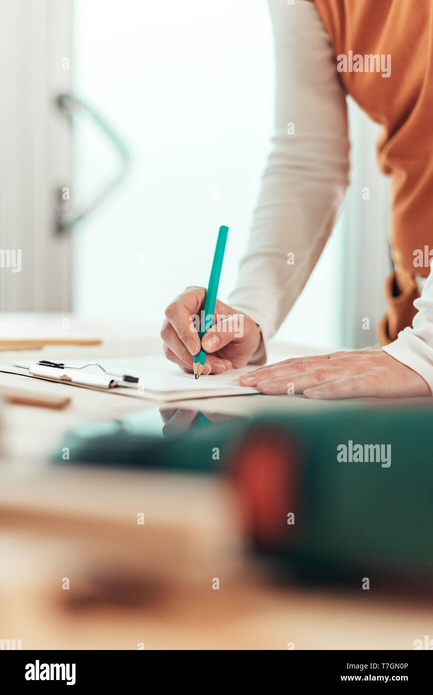 Self employed female carpenter writing project notes on clipboard ...