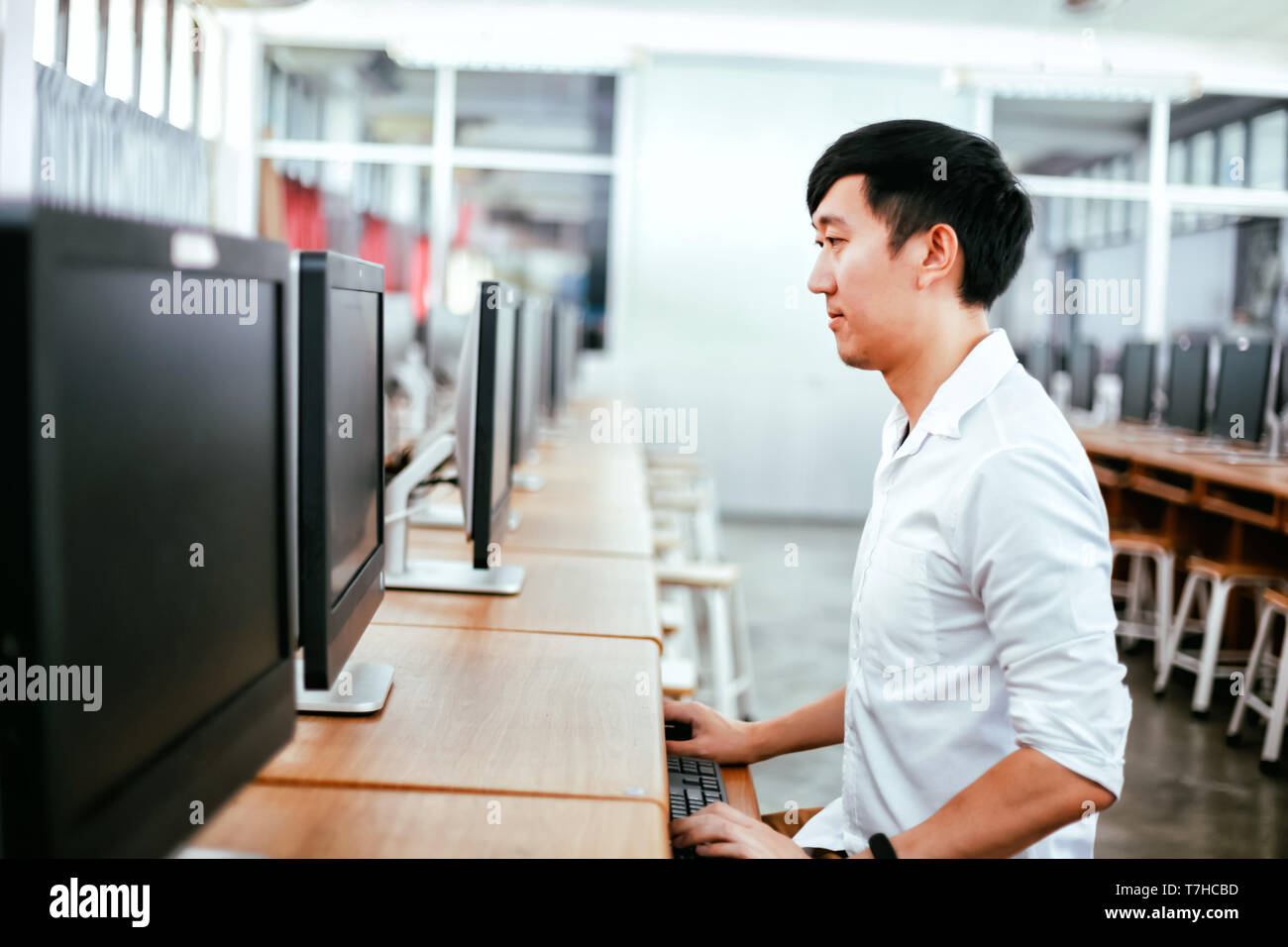 Side view of casual Asian man using computer at desk in modern ...