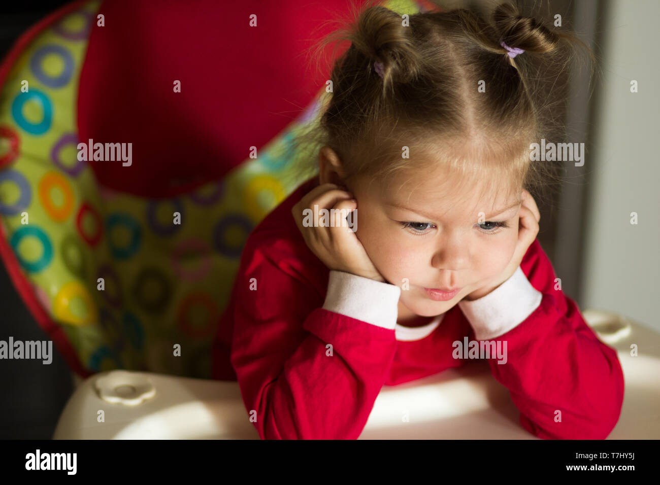 portrait of thinking and sad little girl propping head by hands looking ...
