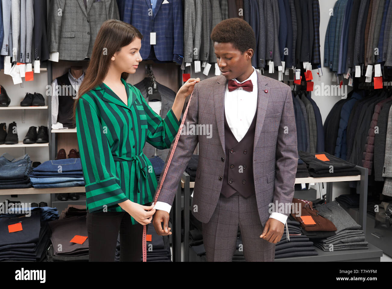 Handsome man fitting grey suit. Pretty shop consultant measuring sleeve ...