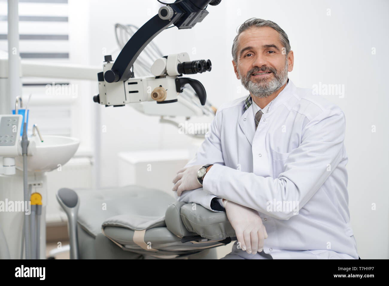 Mature stomatologist posing on workplace, near dental microscope ...