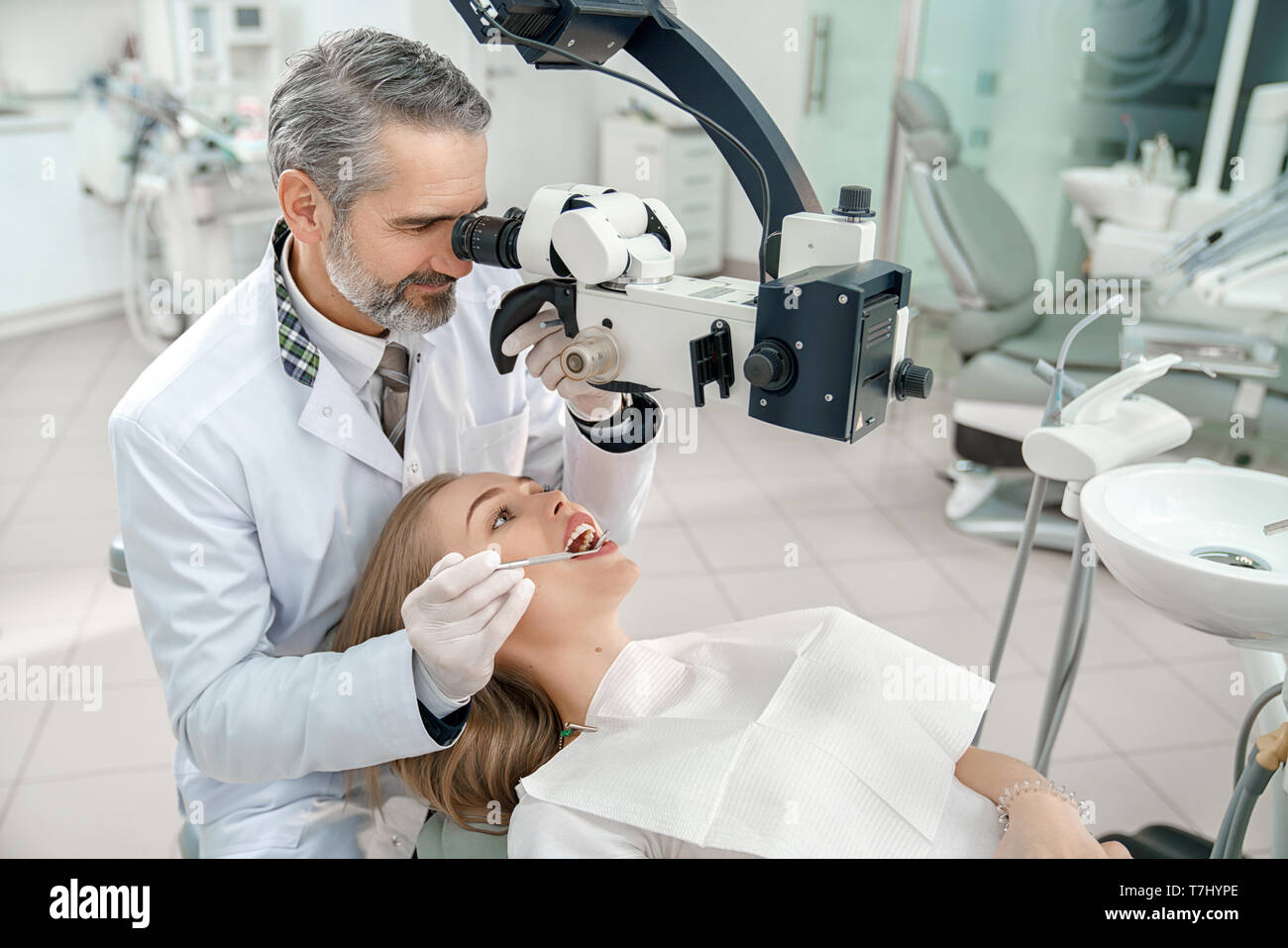 Side view of male dentist looking at microscope and checking teeth of ...