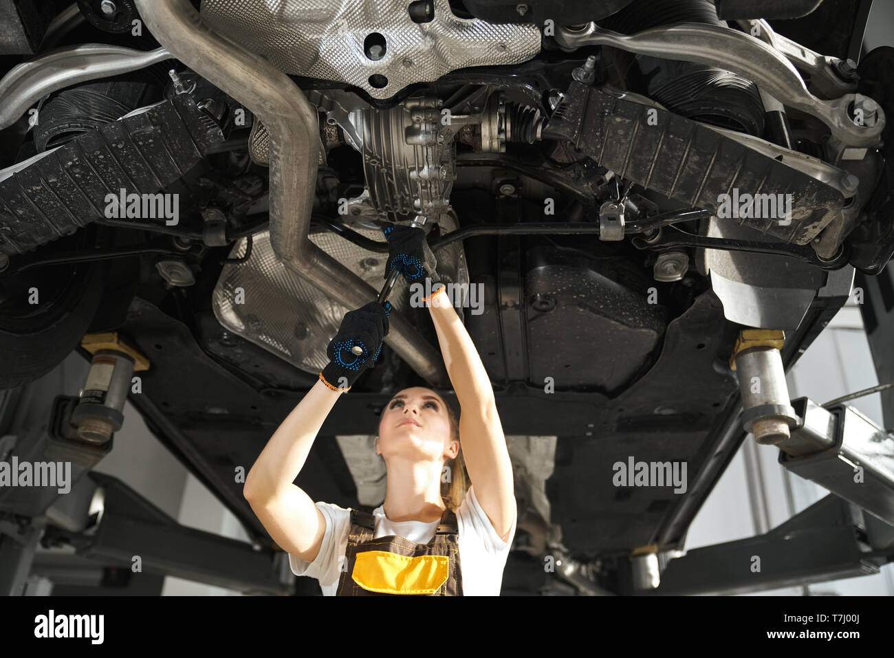 Professional young woman working with undercarriage of automobile ...