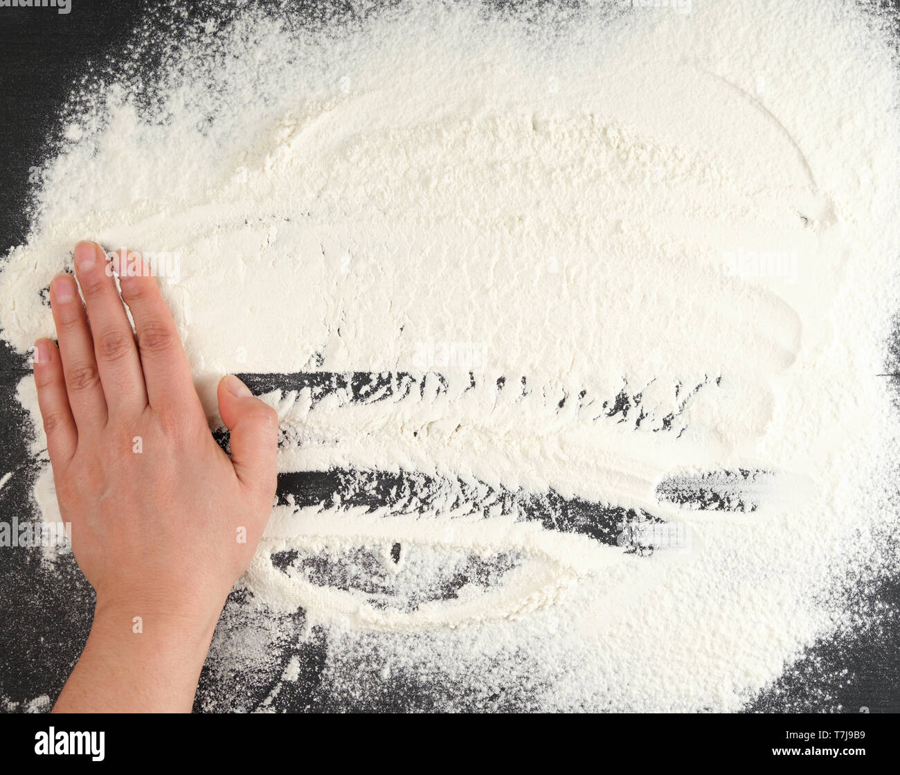 white wheat flour scattered on a black background and female hand ...
