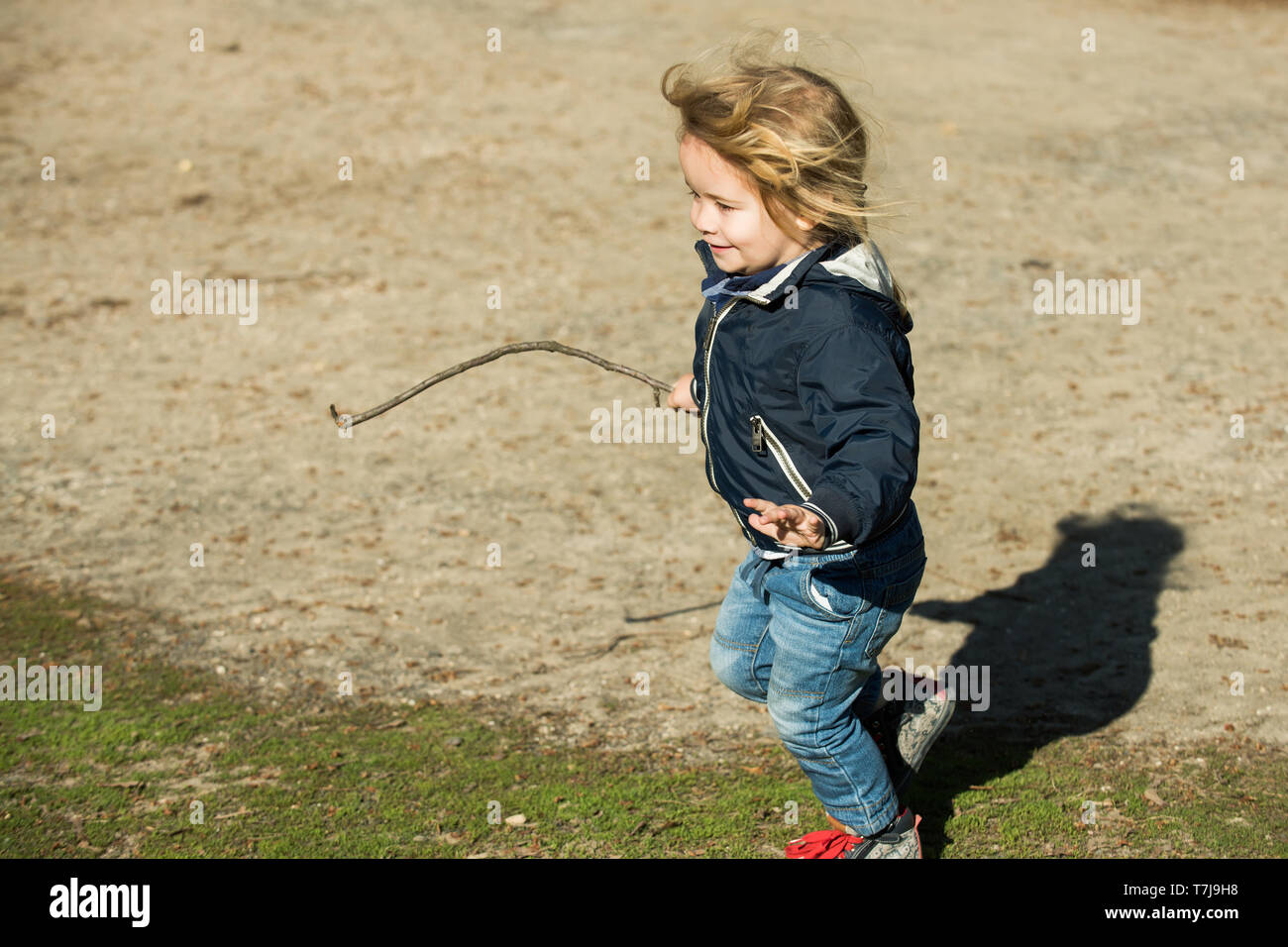 Boy in blue jacket and jeans happy run with stick Stock Photo - Alamy