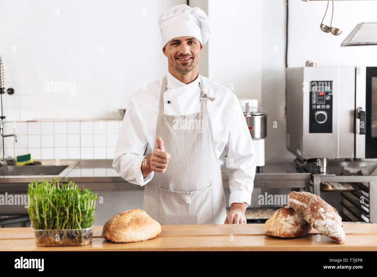 Image of european man baker in white uniform smiling while standing at ...