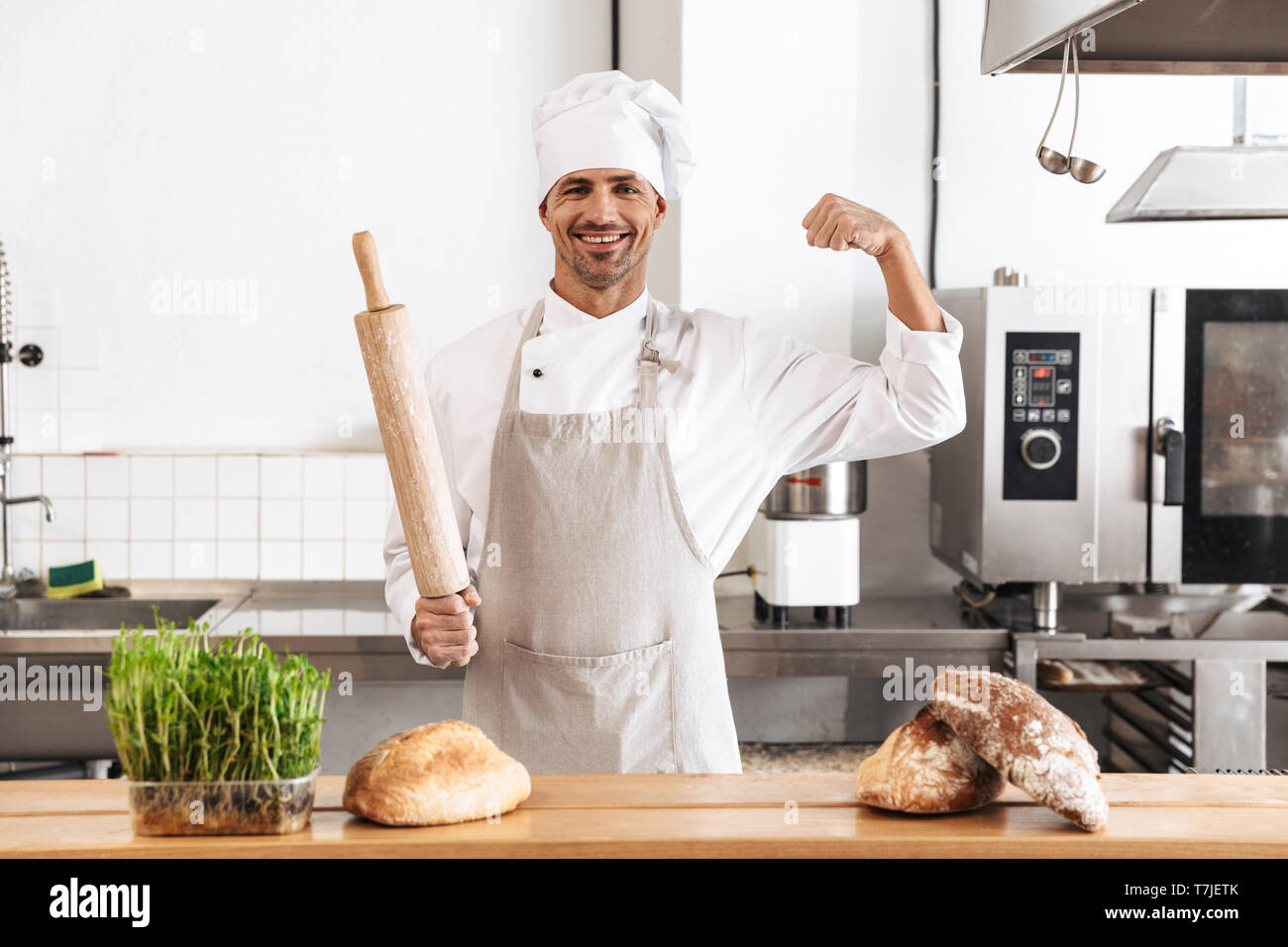 Image of excited man baker in white uniform smiling while standing at ...