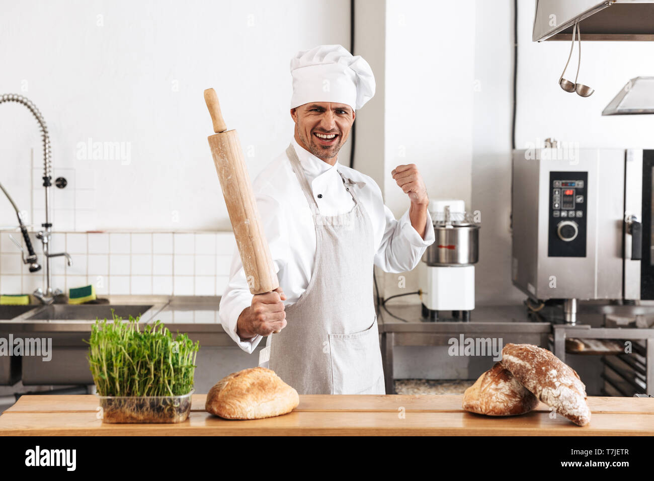 Image of joyous man baker in white uniform smiling while standing at ...
