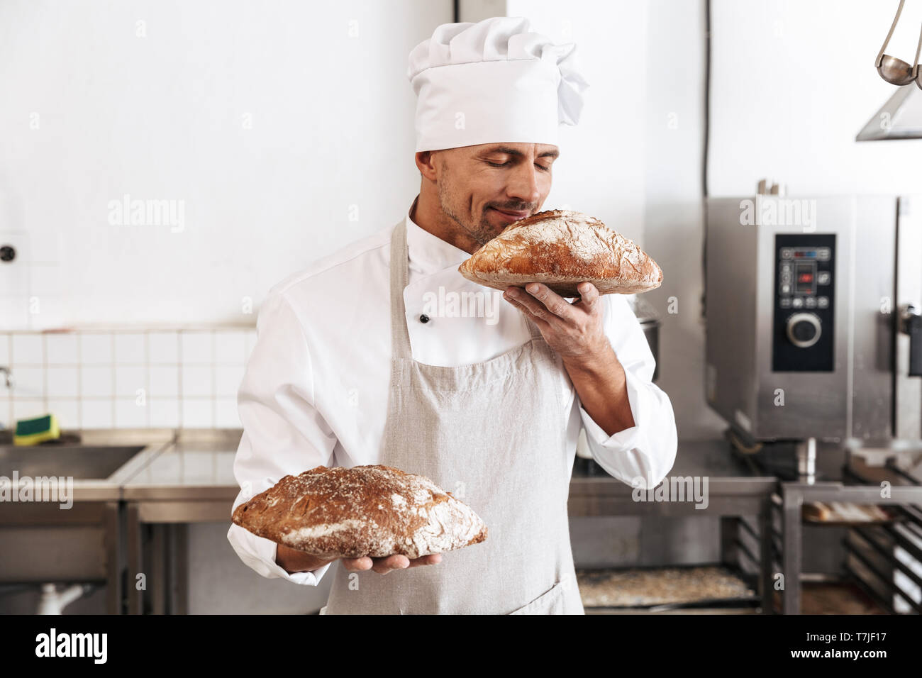 Image of handsome male baker in white uniform standing at bakery and ...
